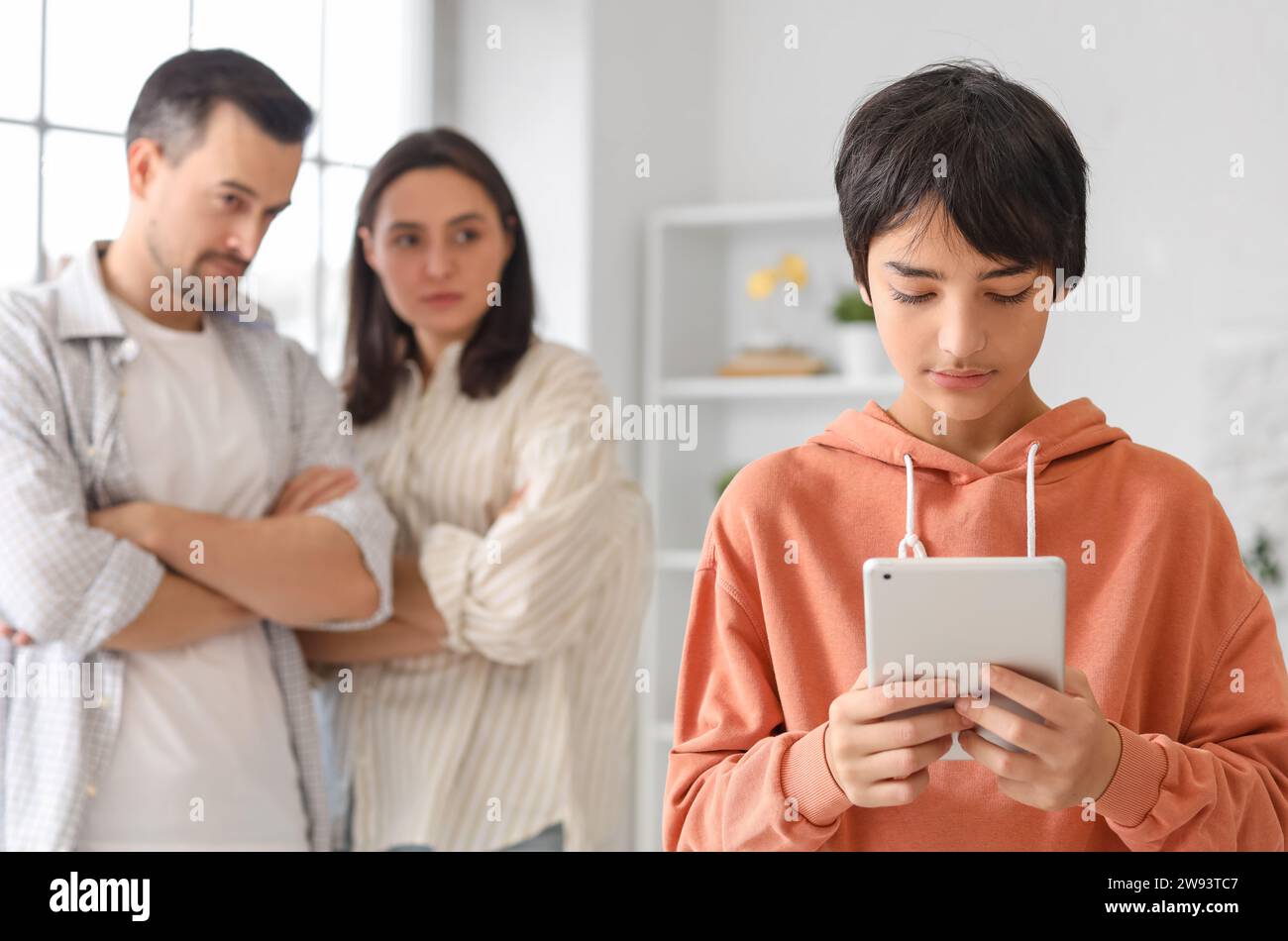 Teenage boy using tablet computer and his unhappy parents at home ...