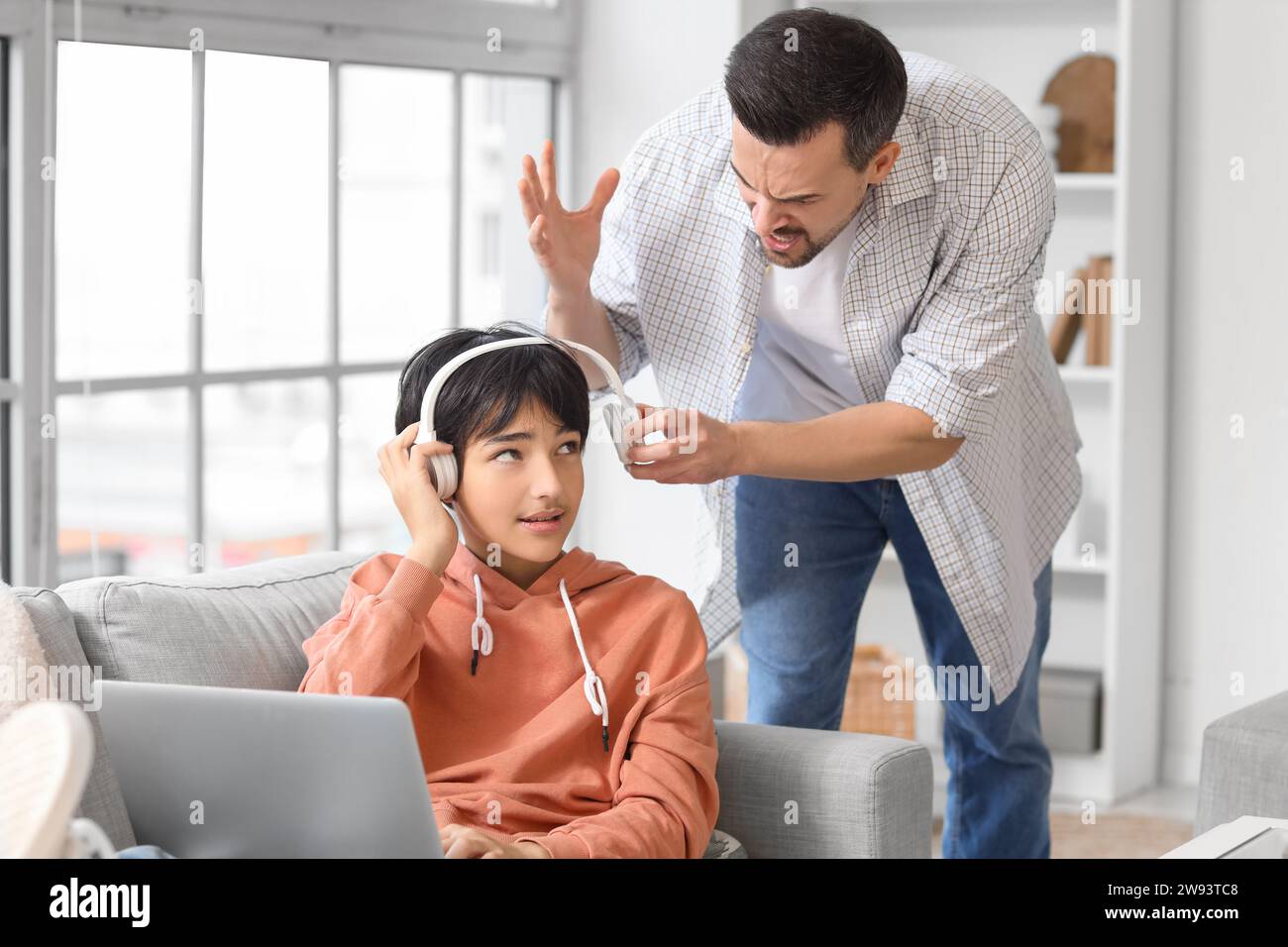 Angry father arguing with his teenage son in headphones at home. Family problem concept Stock ...