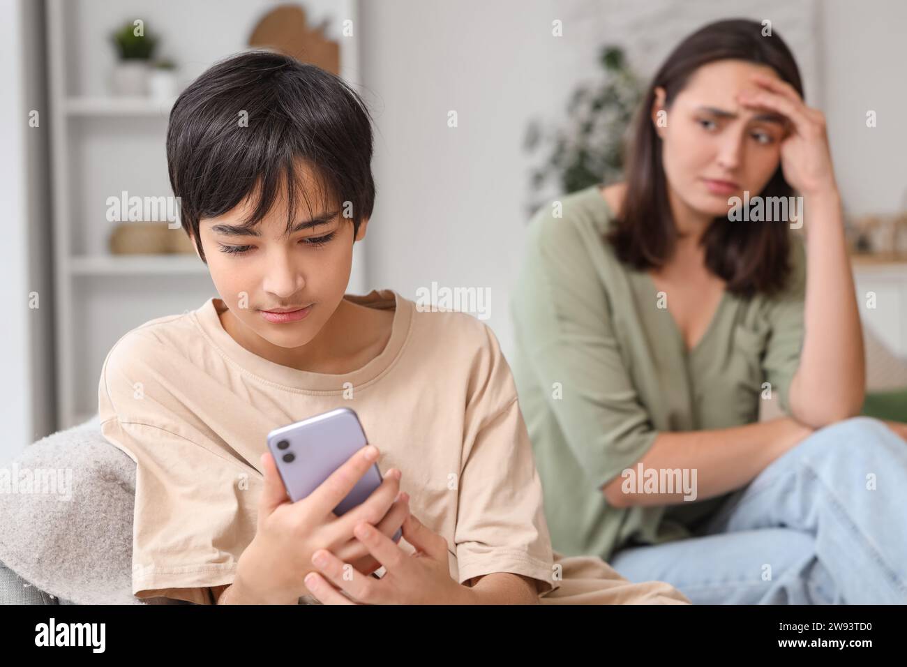 Teenage boy using mobile phone and his upset mother at home. Family ...