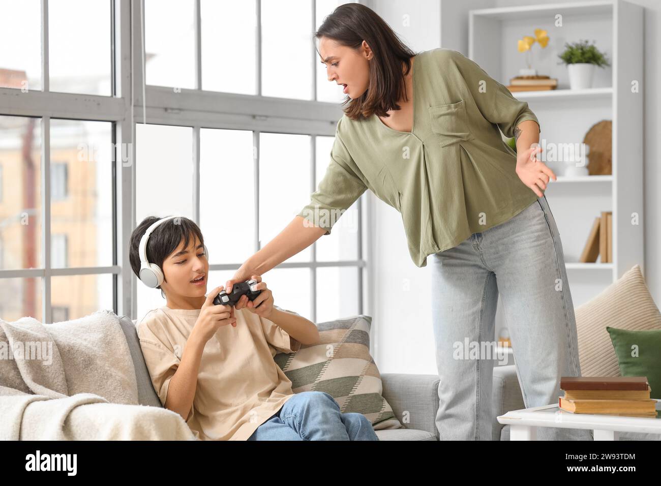 Angry mother taking game pad away from her teenage boy at home. Family ...