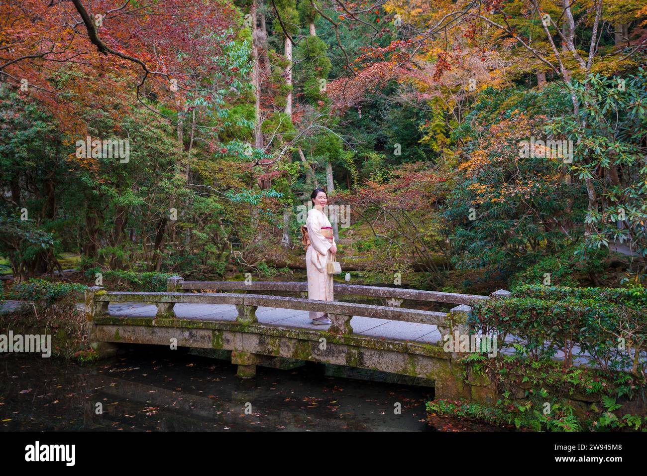 A woman wearing kimono standing on a Japanese style stone arch bridge ...