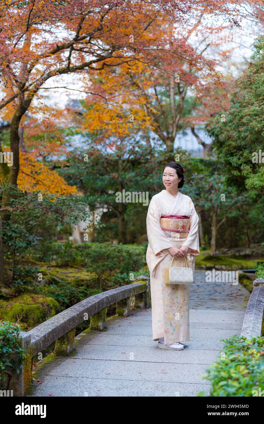 A woman wearing kimono standing on a Japanese style stone arch bridge ...