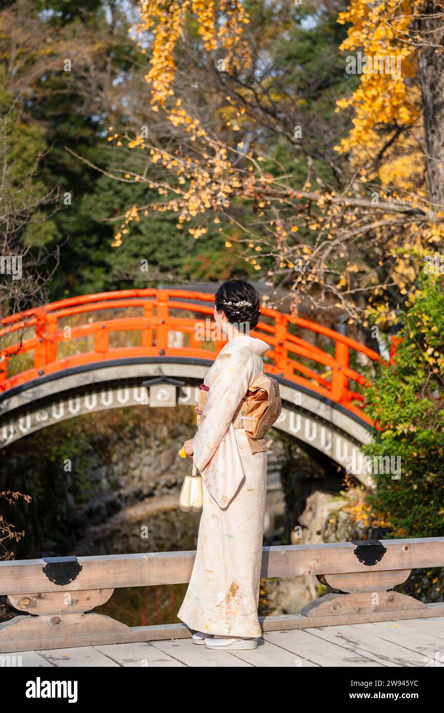 A woman wearing kimono standing in front of a Japanese style arch ...