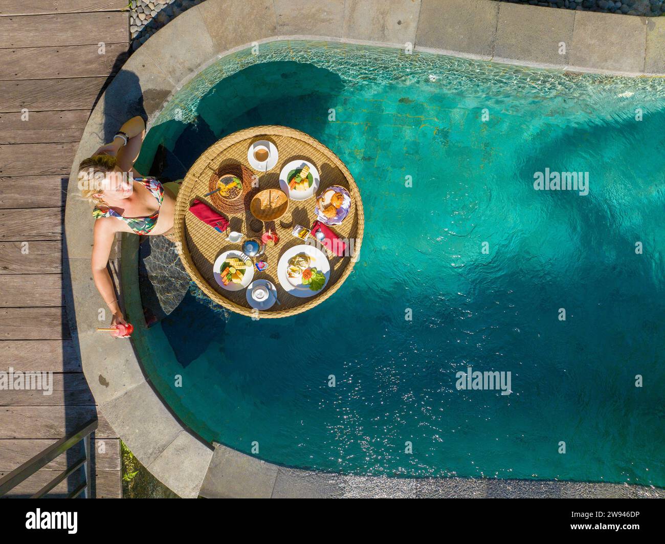 Aerial view of a young woman having breakfast on a floating basket in a ...
