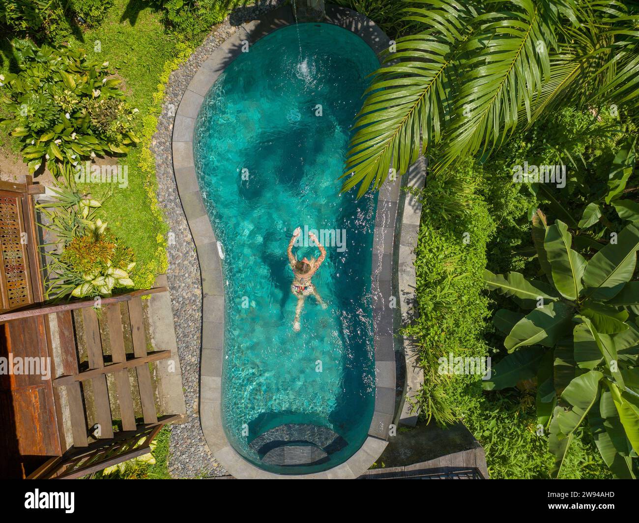 Aerial view of a young woman relaxing in a swimming pool, rural Bali ...