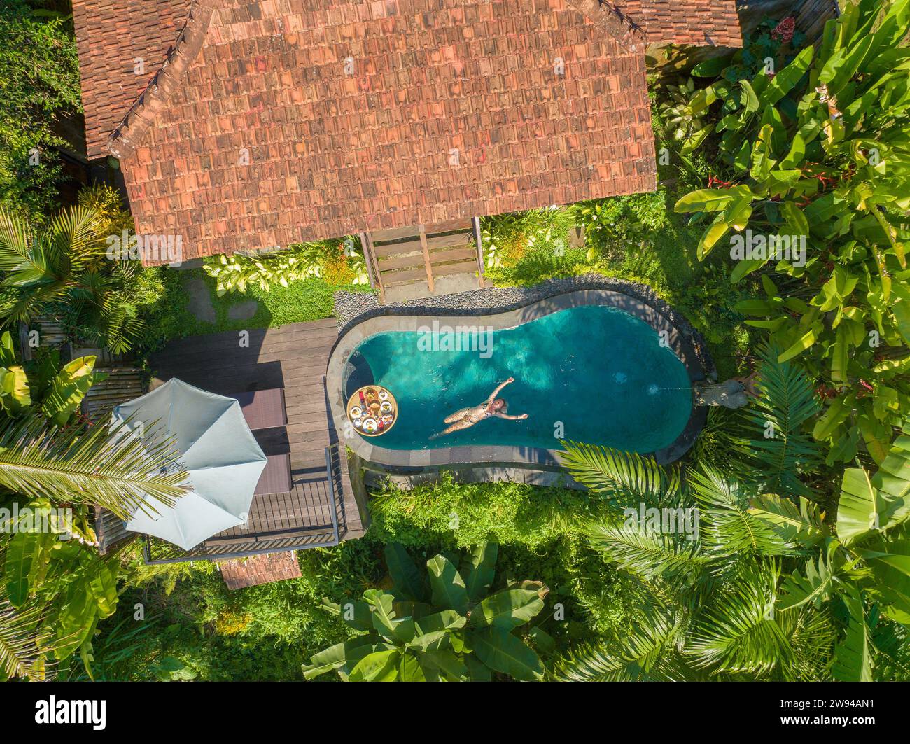 Aerial view of a young woman relaxing in a swimming pool, rural Bali ...