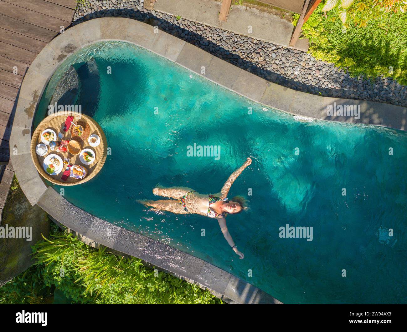 Aerial view of a young woman relaxing in a swimming pool, rural Bali ...