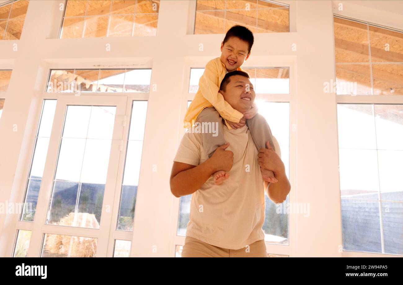 Laughing Asian dad and son have fun together at home. A cute little boy ...