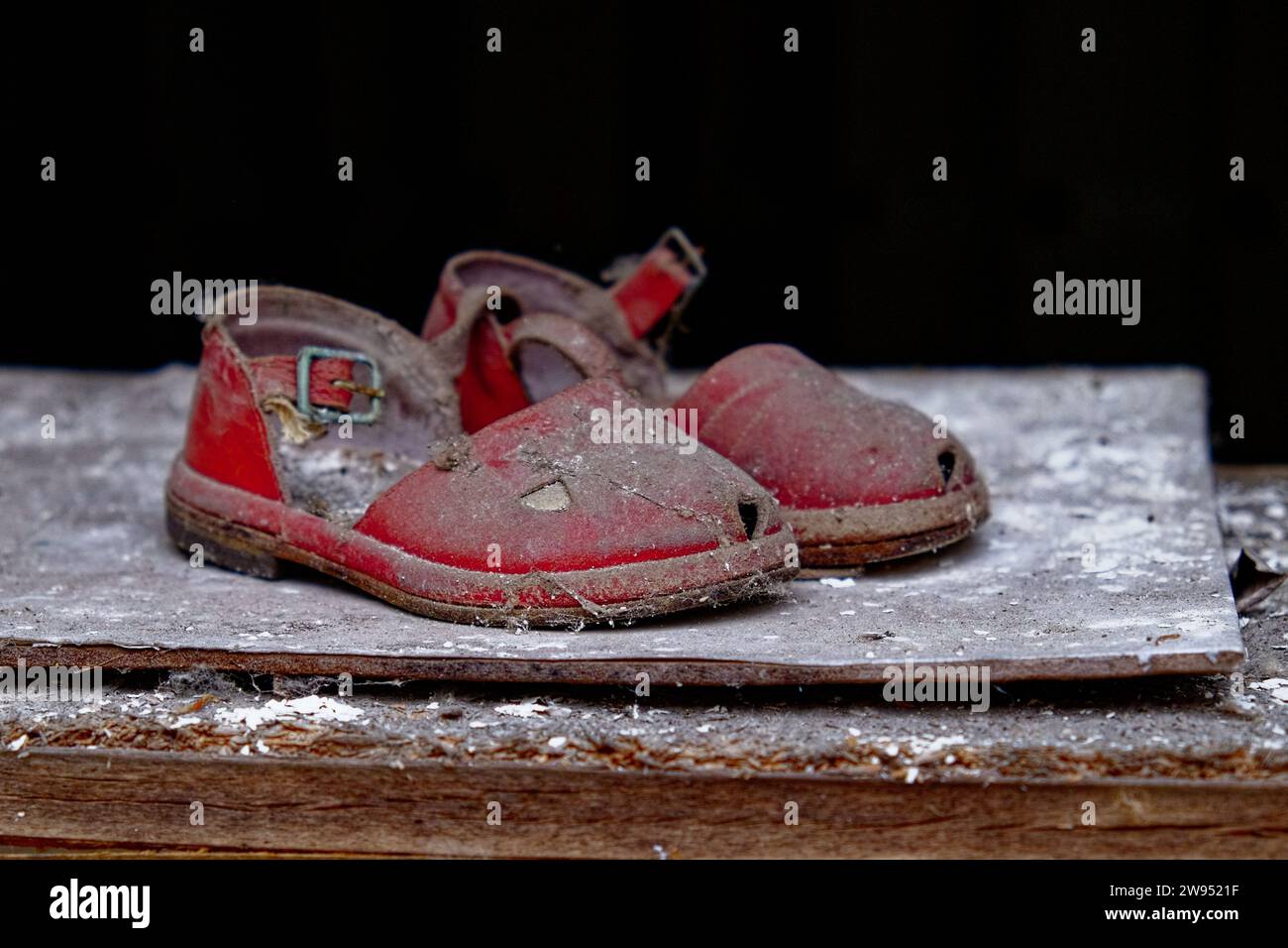 Two worn-out red sandals with buckles, lying on a dusty and dirty ...