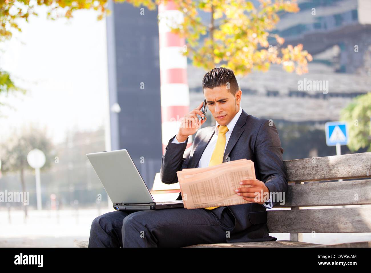 Businessman sited in a bench working with his laptop, calling at the ...