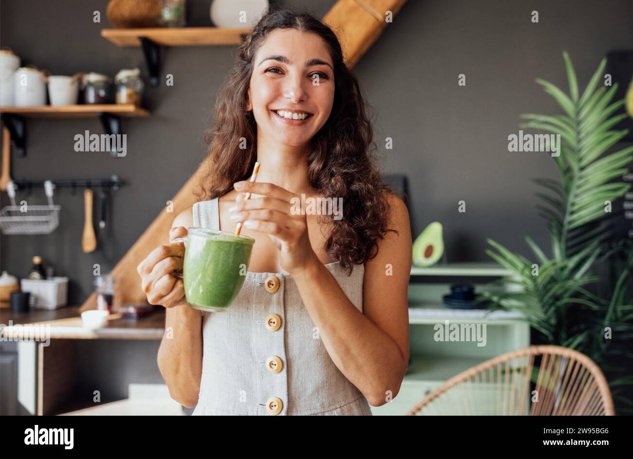 Attractive curly-haired girl in white top smiles and drinks green ...