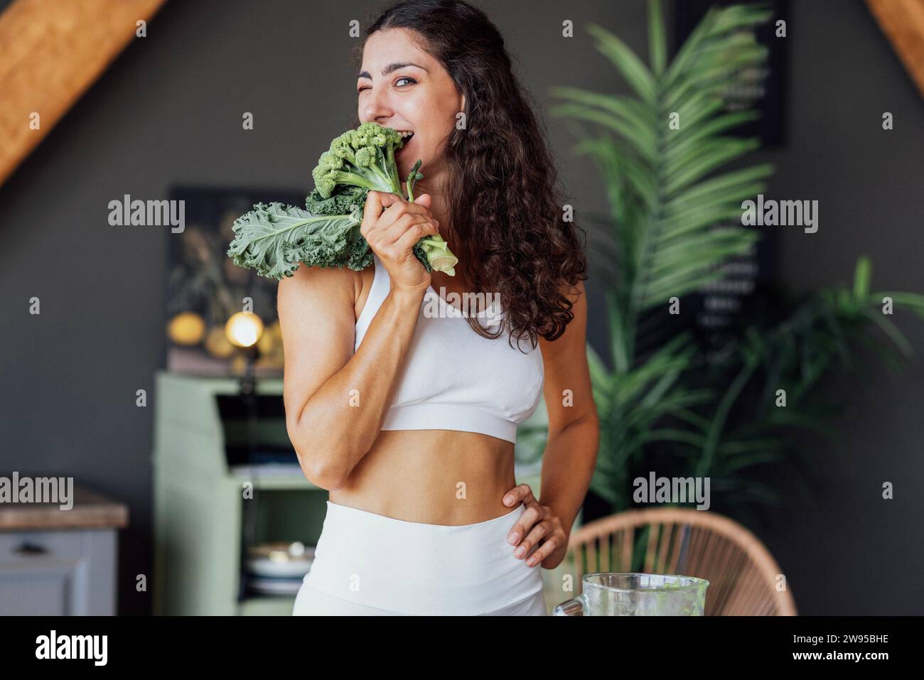 An attractive smiling vegan girl in a white top bites fresh broccoli. A ...
