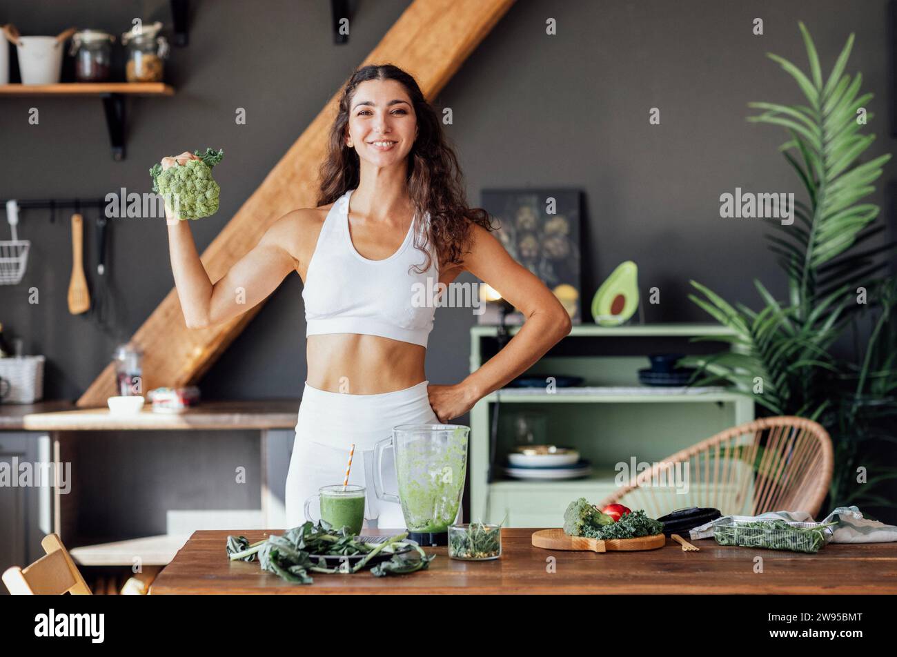 An attractive smiling vegan girl in a white top bites fresh broccoli. A ...