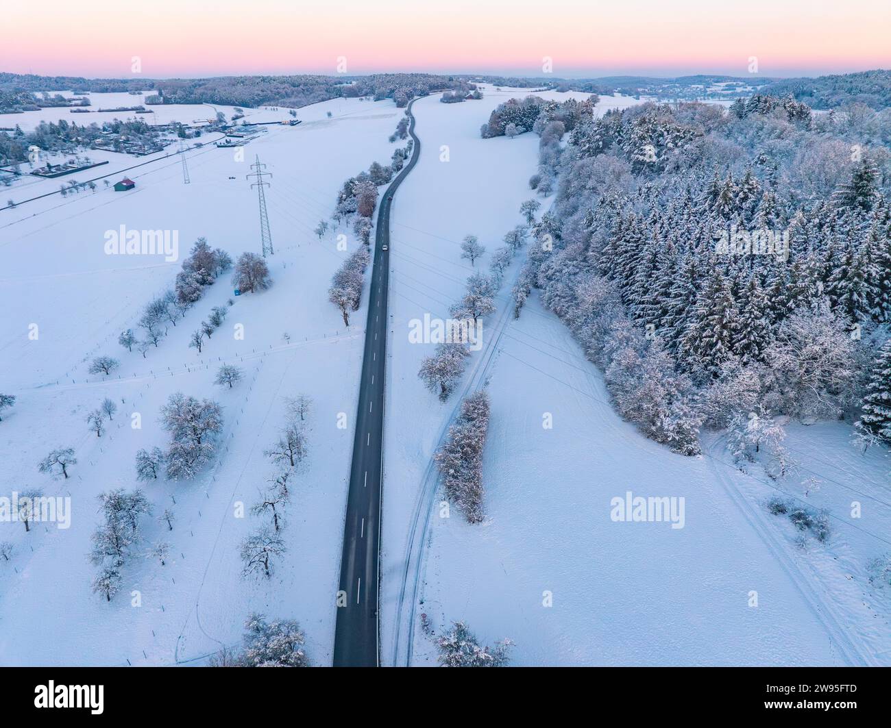 Snow-covered road winds through a quiet forest at dusk, aerial view ...