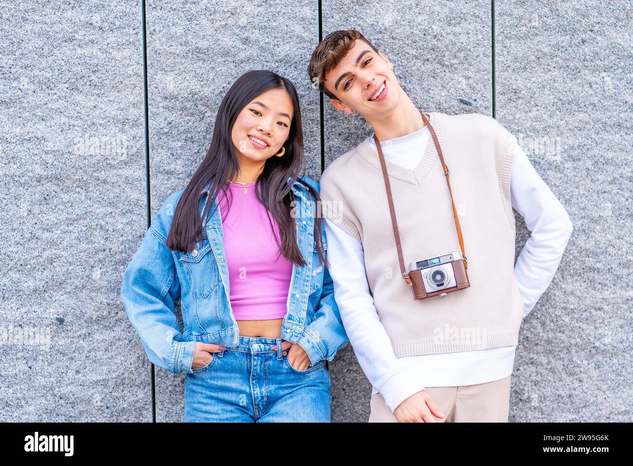 Frontal portrait of two multi-ethnic young friends leaning on a wall ...