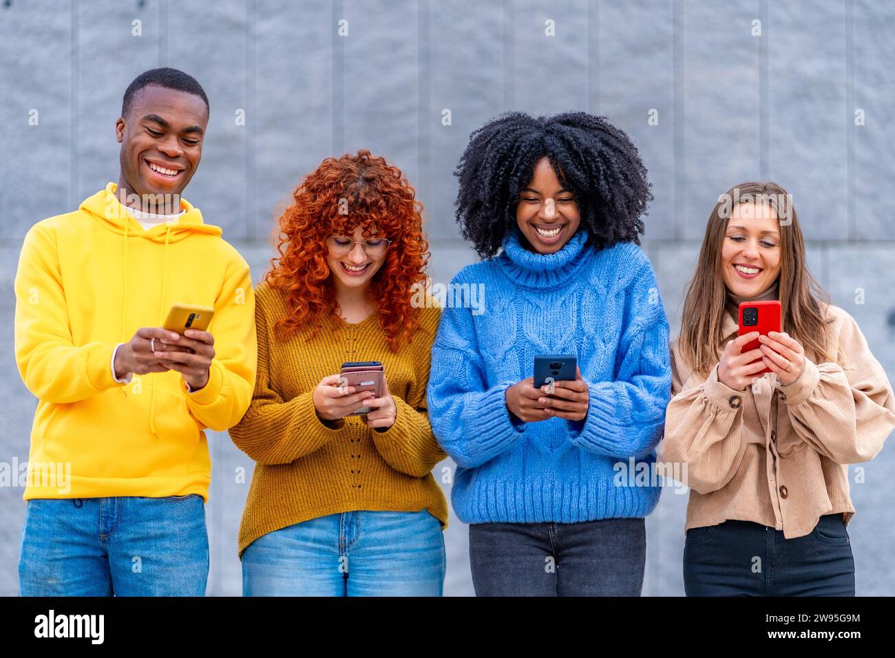Frontal portrait of smiling young diverse people using phone standing ...