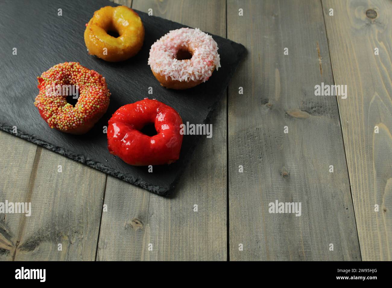 Four multicolored red, yellow, white, pink donut on a stone on a gray ...