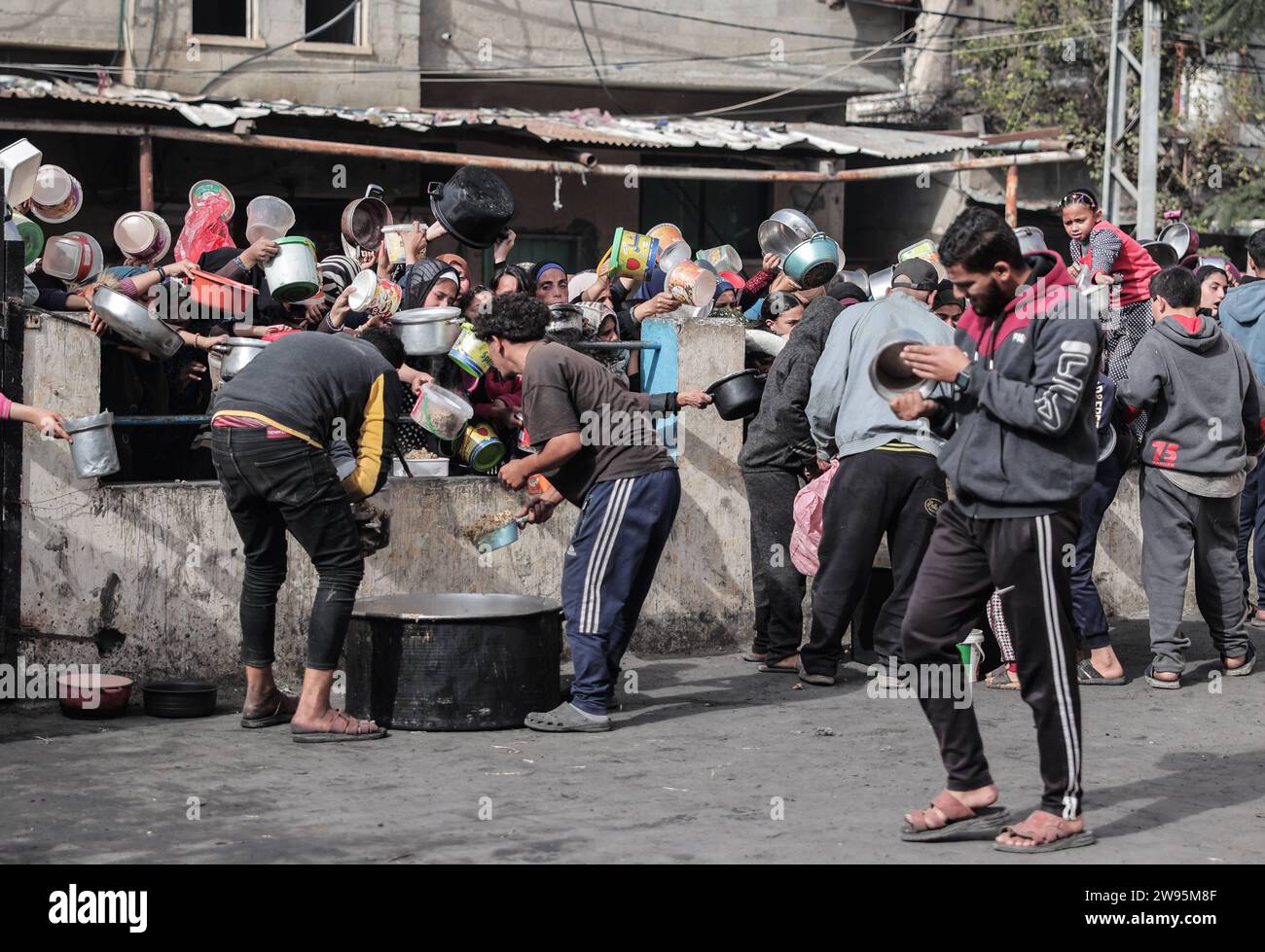 Palestinians wait to collect food at a donation point in a refugee camp ...