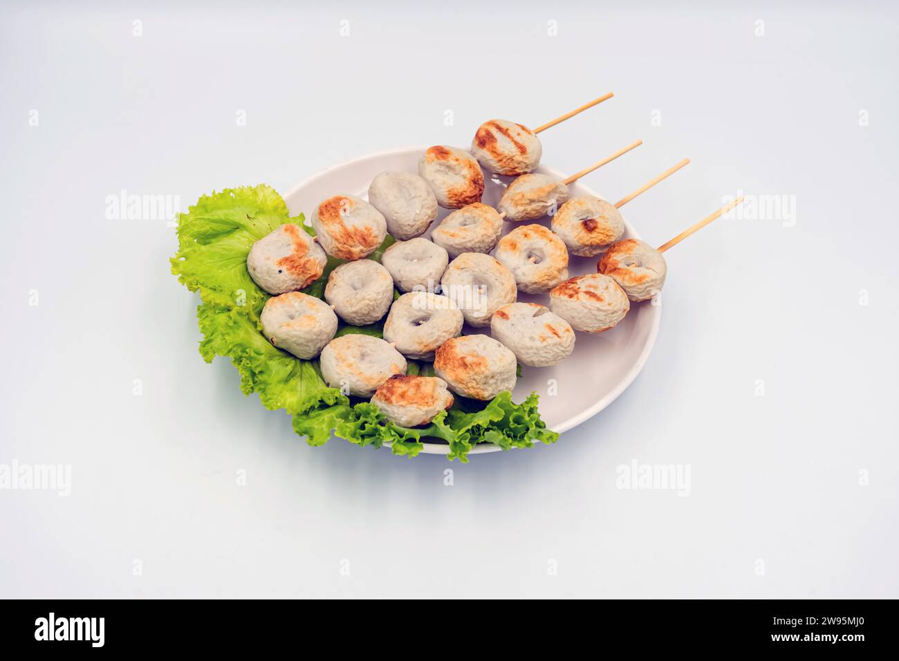 Tasty roasted fish meatballs skewers and lettuce on dish with white ...
