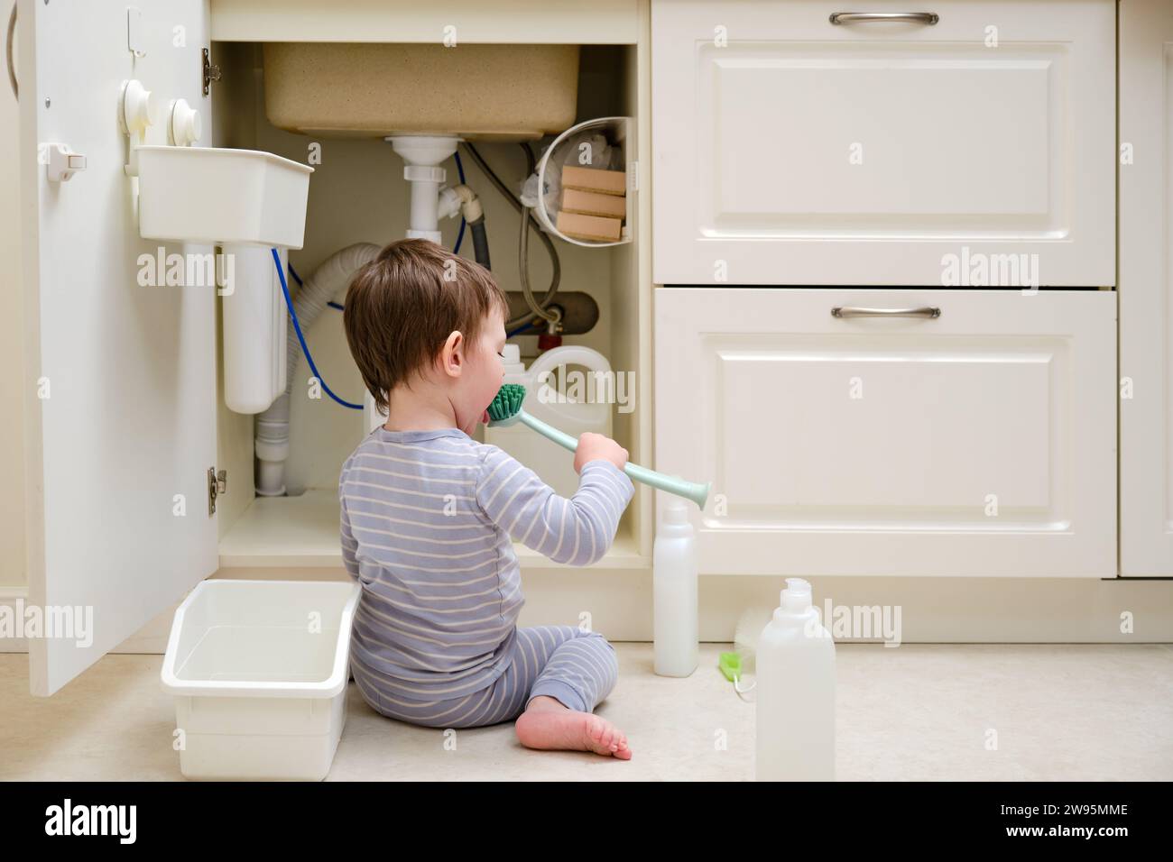 A child is playing with chemical cleaning products under the sink in ...