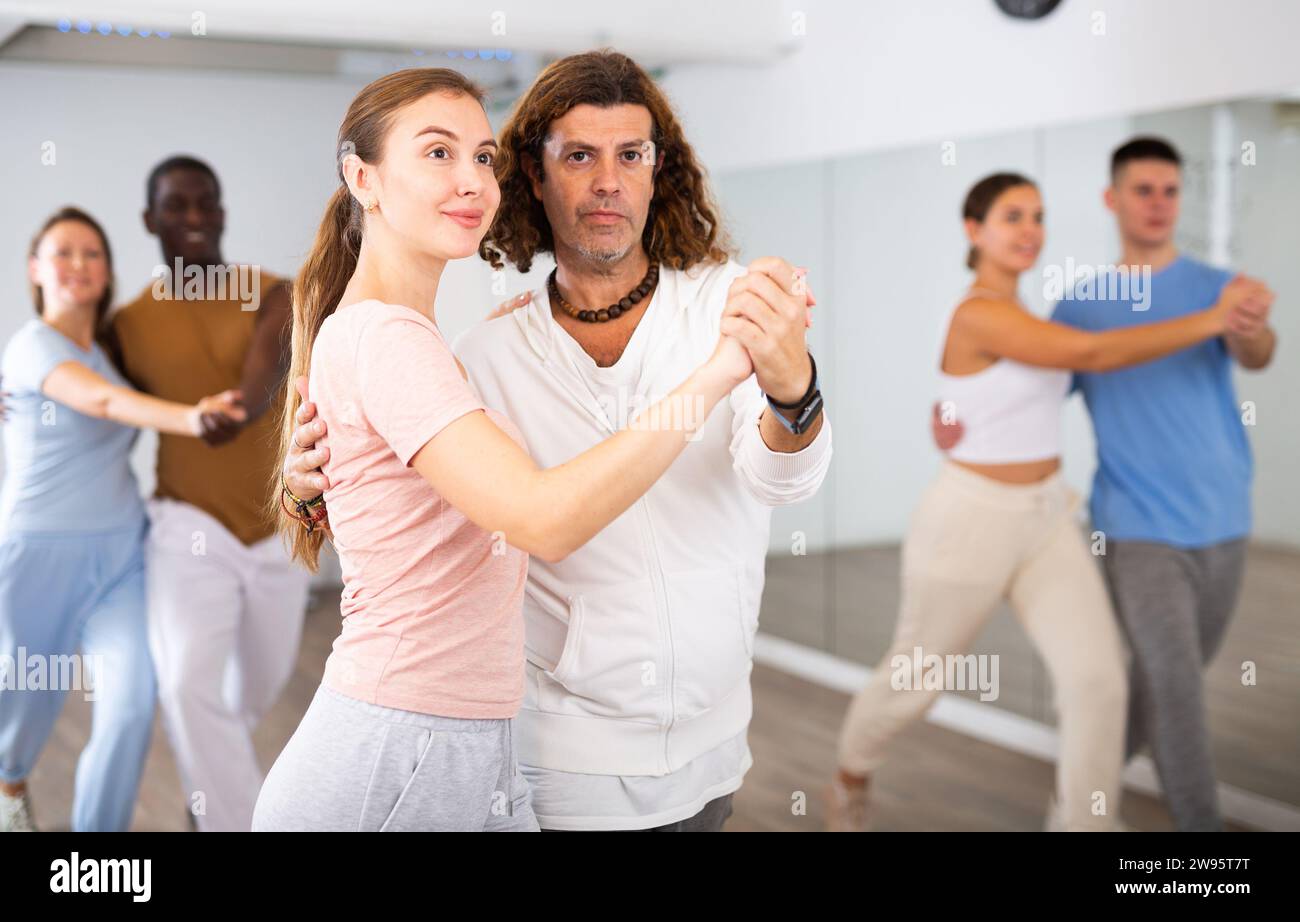 Smiling dancing people practicing movements while dancing in pairs in ...