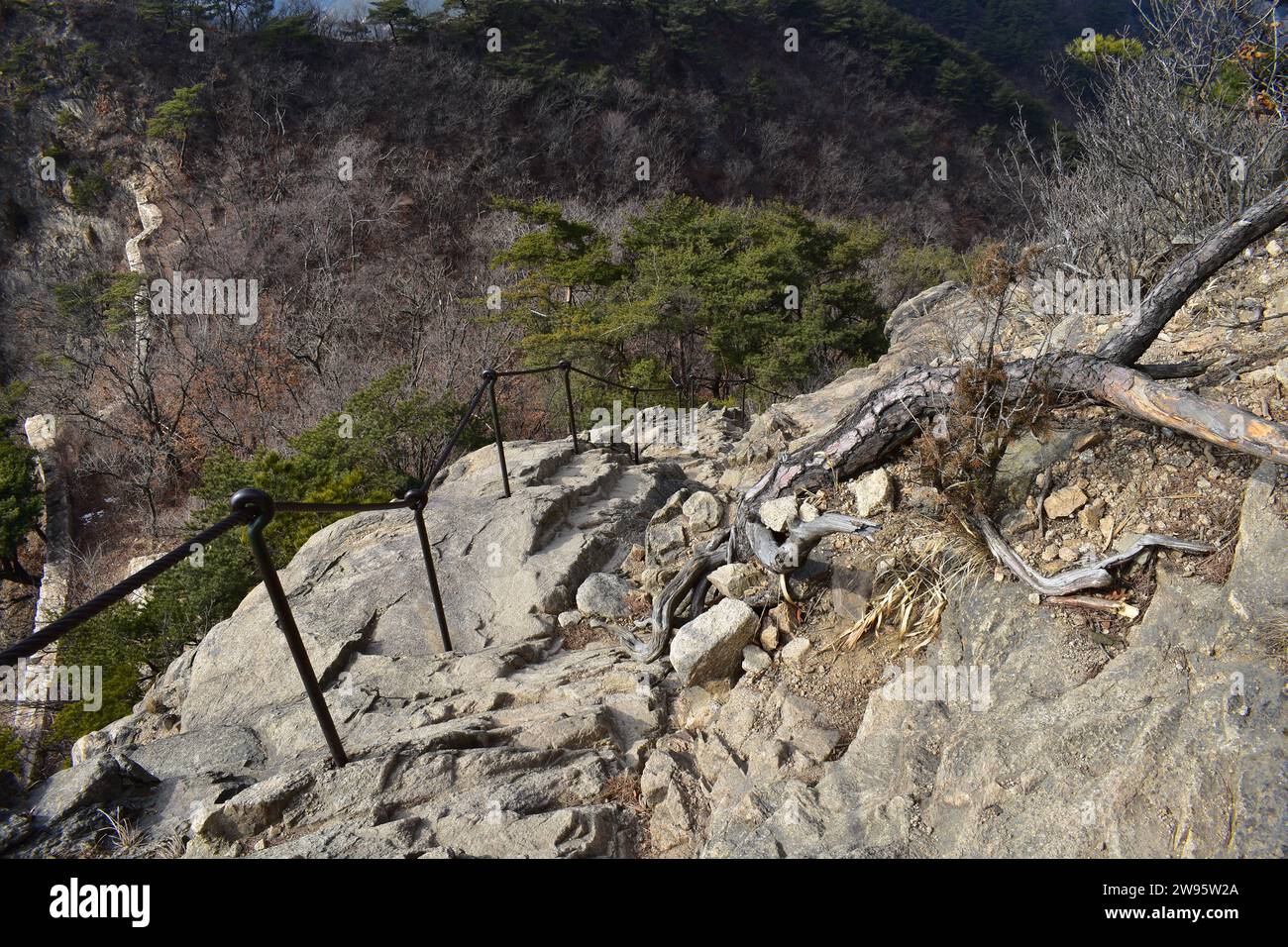 A rough and rocky mountainside hiking trail fenced off by a steel hand ...