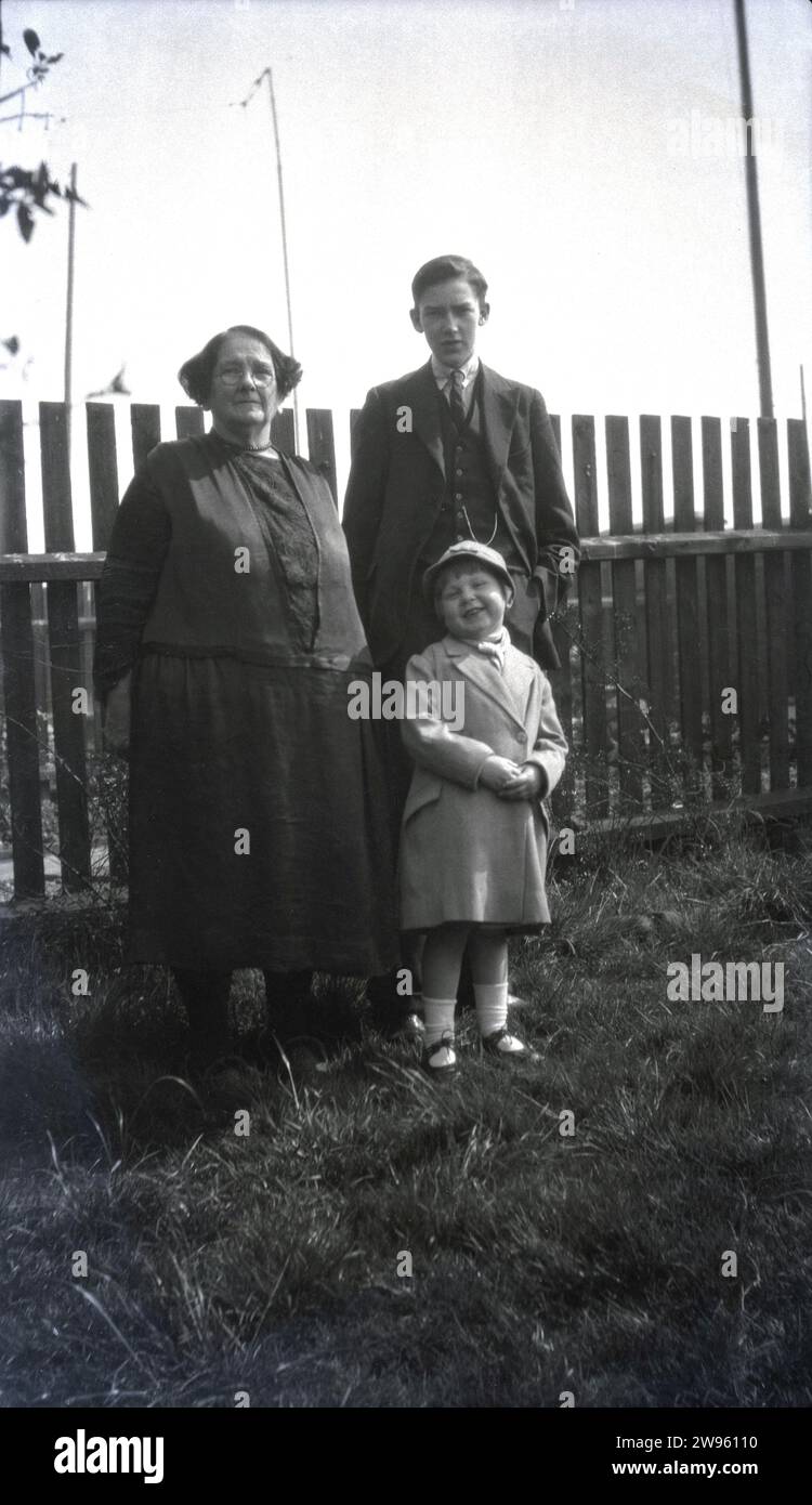 1950s, historical, standing by a wooden fence, a rotund grandmother ...