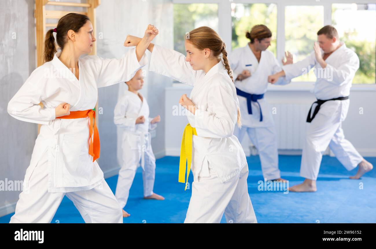 Young girl and woman in kimono and colored belt practicing karate punch ...