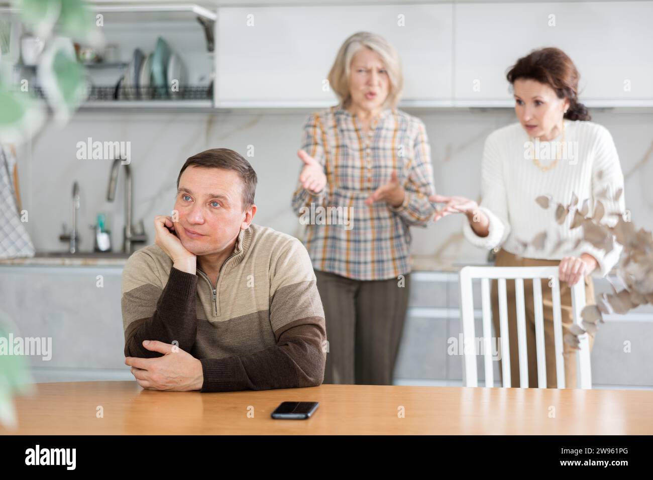 Old and middle-aged woman quarreling angrily to man sitting at the ...