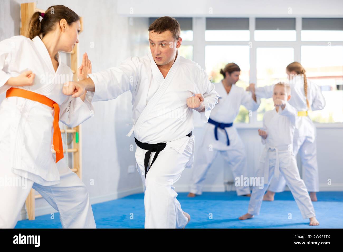 Focused woman in kimono practices combat technique of punching and blocking with trainer at ...