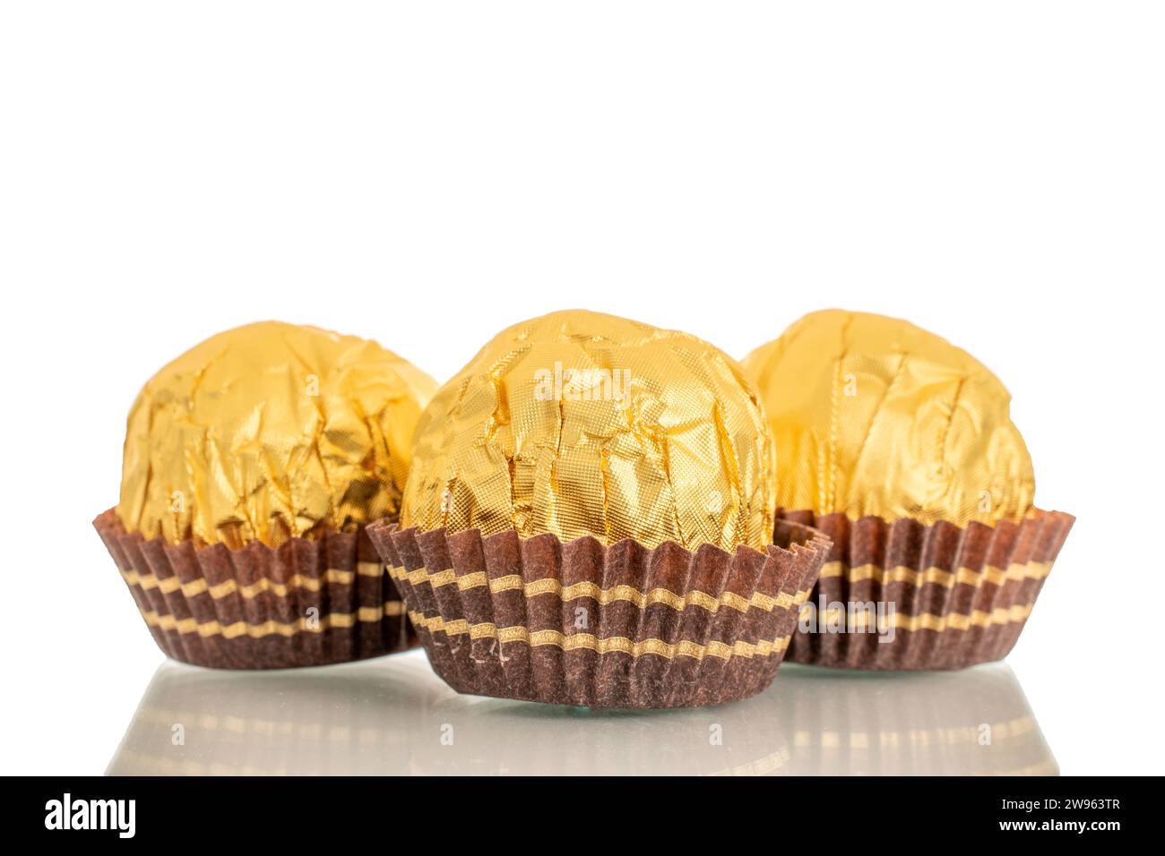Three chocolate candies with a nut in a paper wrapper, macro, isolated ...