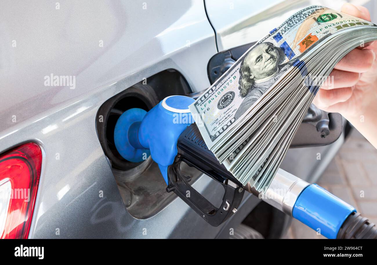 Gasoline pump gun to release fuel into passenger car and stack of american dollars in the hand ...