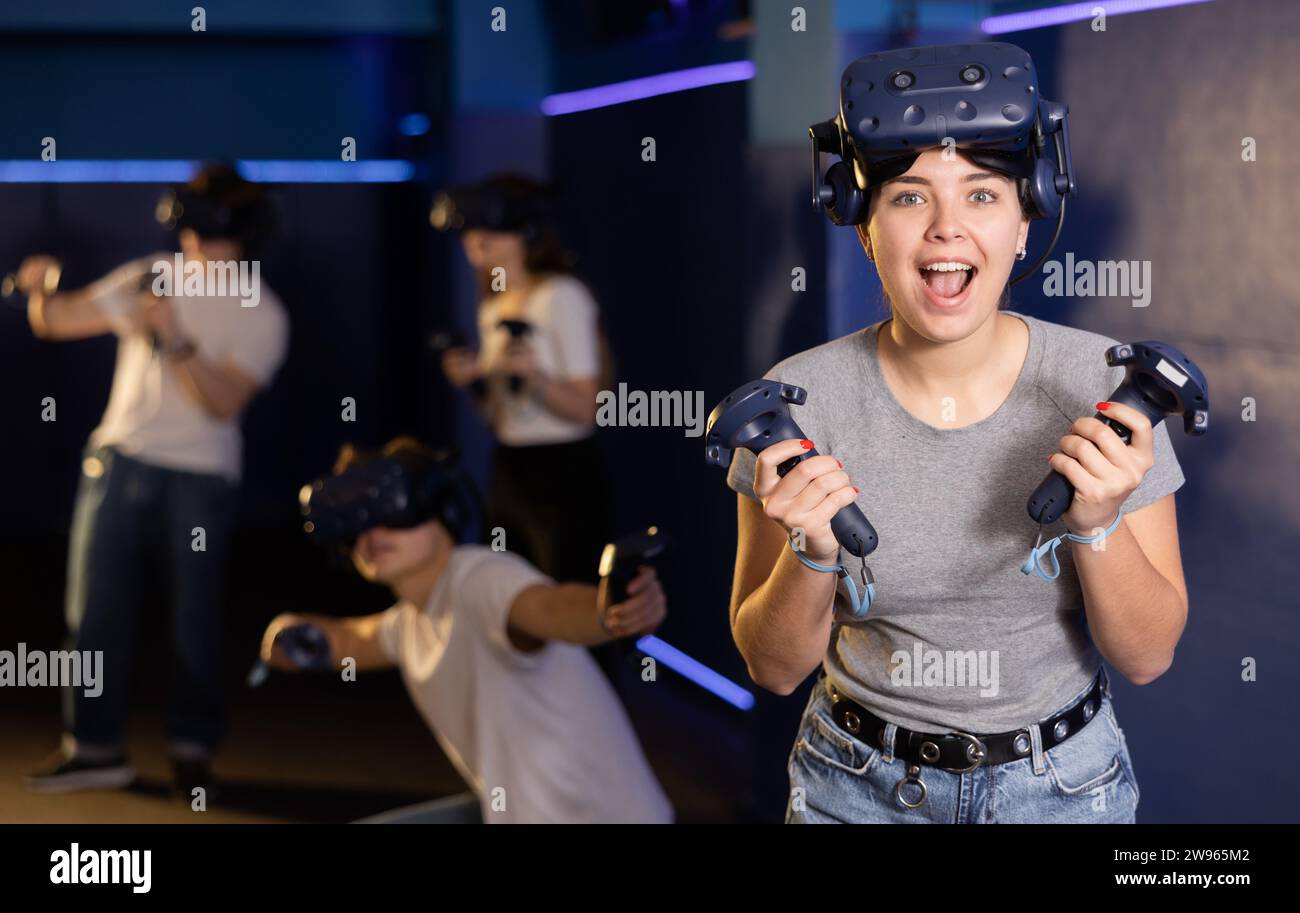 Excited girl with gaming controllers and VR goggles in virtual reality ...