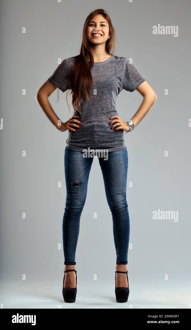Young woman stands confidently in skinny jeans and heels, her smile as ...