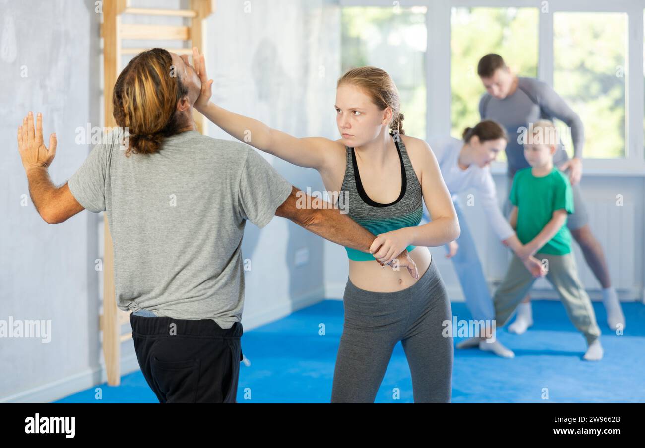 Girl and man in group self-defense classes practicing sparring technique of blowing to chin in ...