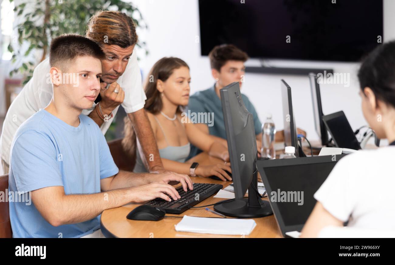 During computer lesson, male teacher helps guy student complete ...