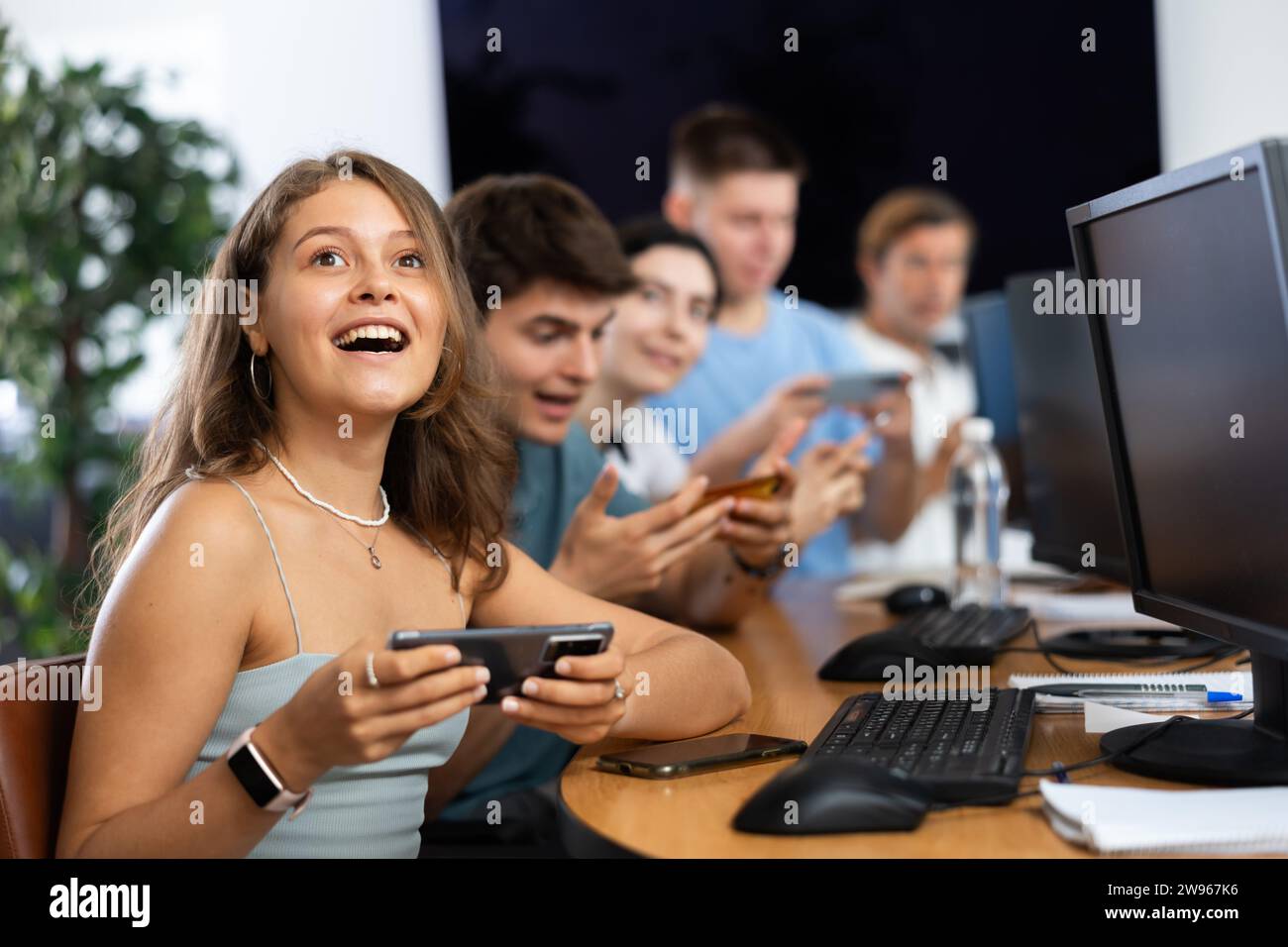 At computer class, young girl student sits with mobile phone and ...
