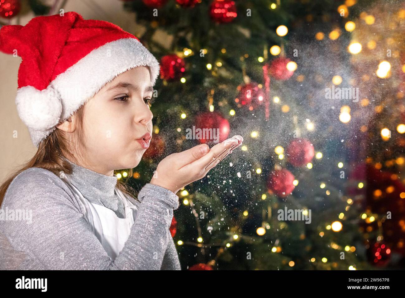 A girl in a Santa hat blows magic dust from her palm against the ...