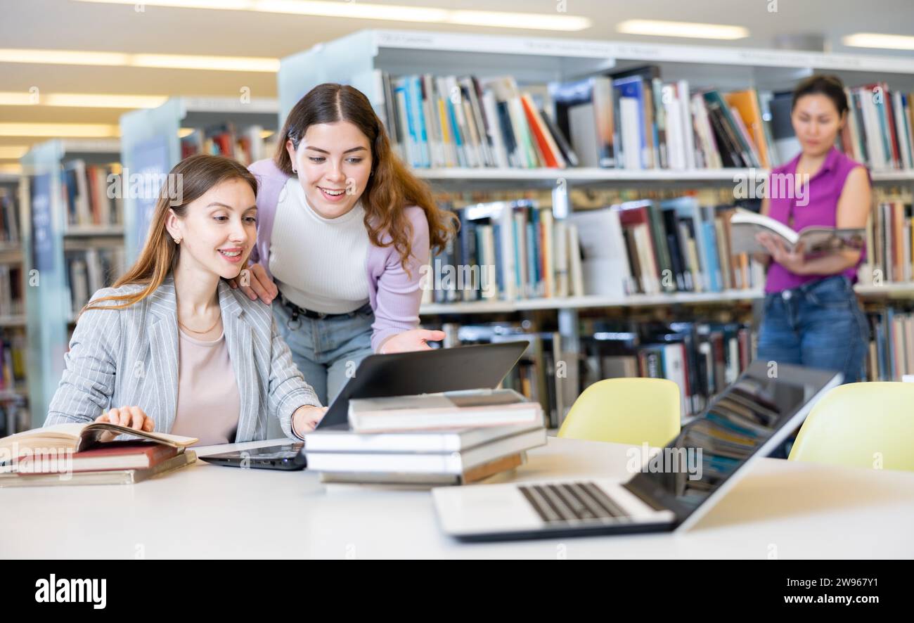 Two positive women working with books and laptop in library Stock Photo ...