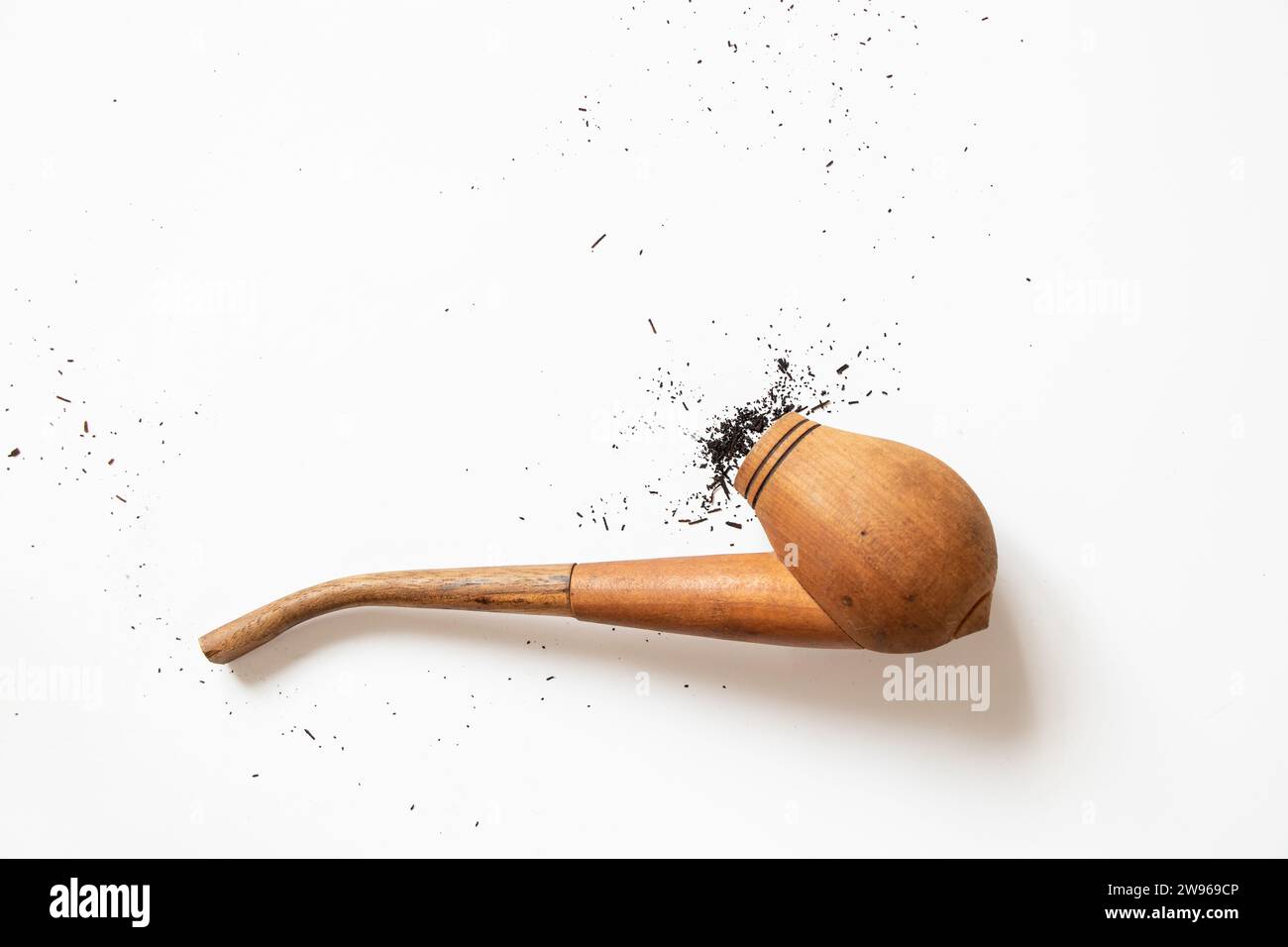 A smoking pipe and ashes scattered around lie on a white background ...