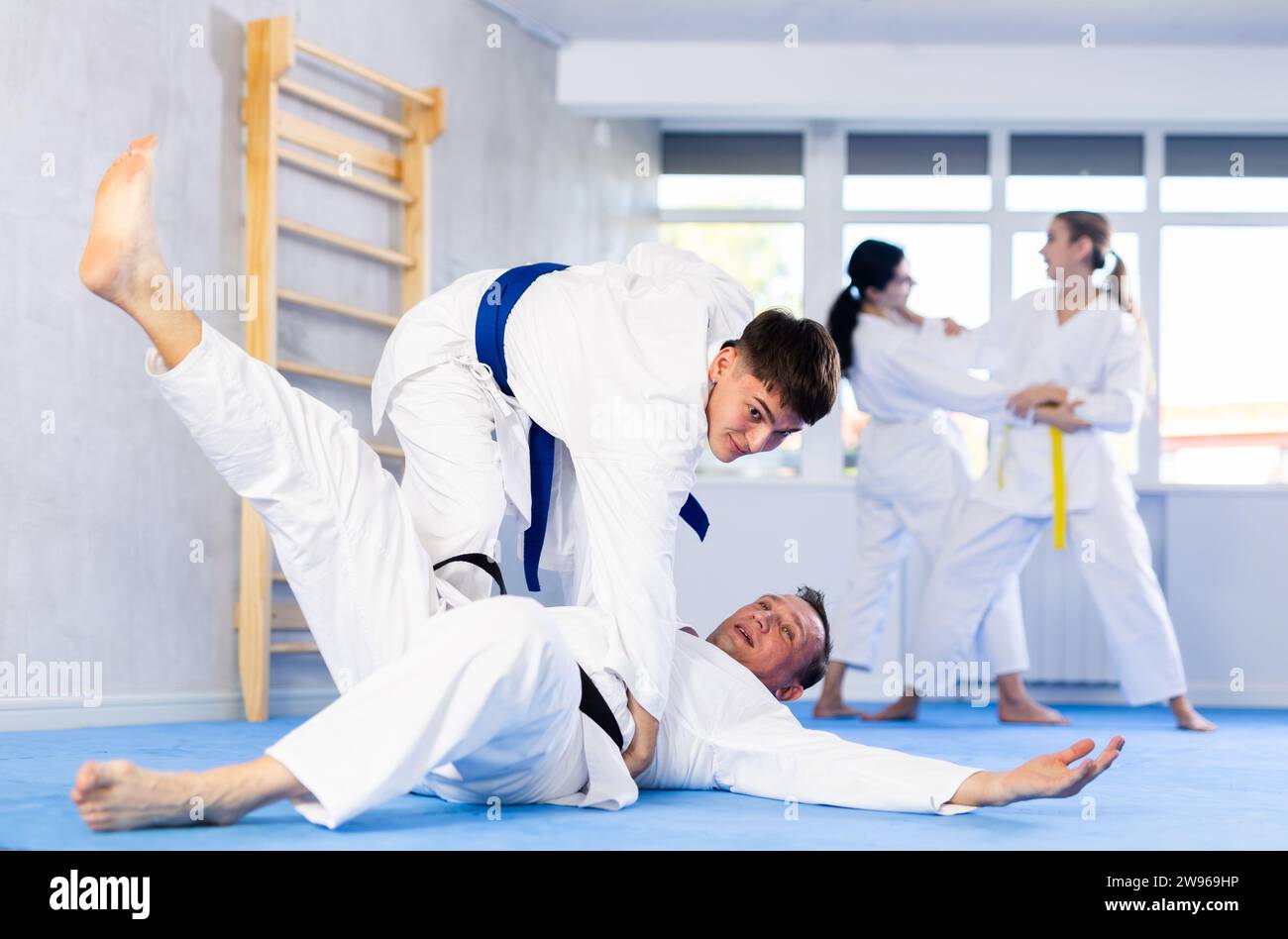Adult man and young guy in kimonos train judo techniques in group in ...