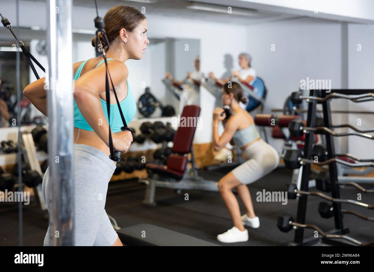 Young girl trainer in hall of gym fitness center works with muscles of ...
