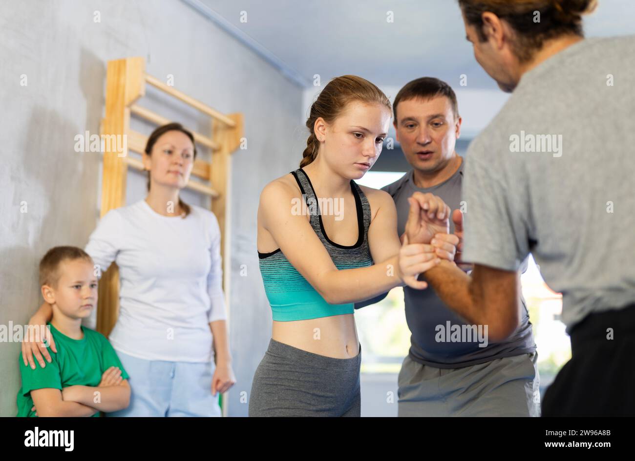 Trainer on man explains palm grab technique, boy, girl and woman watch ...