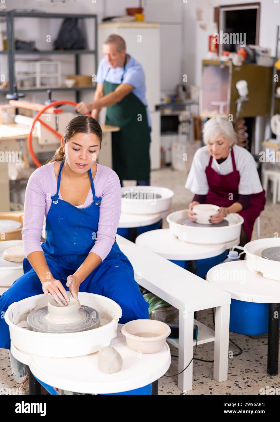 Young woman learning to work on potter wheel and making pitcher throat ...