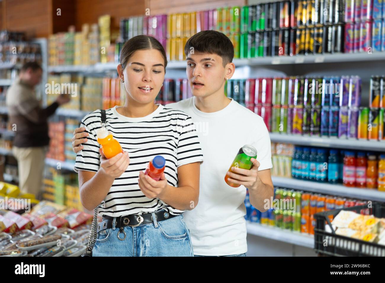 Interested smiling young girl and guy choosing soft drinks in grocery ...