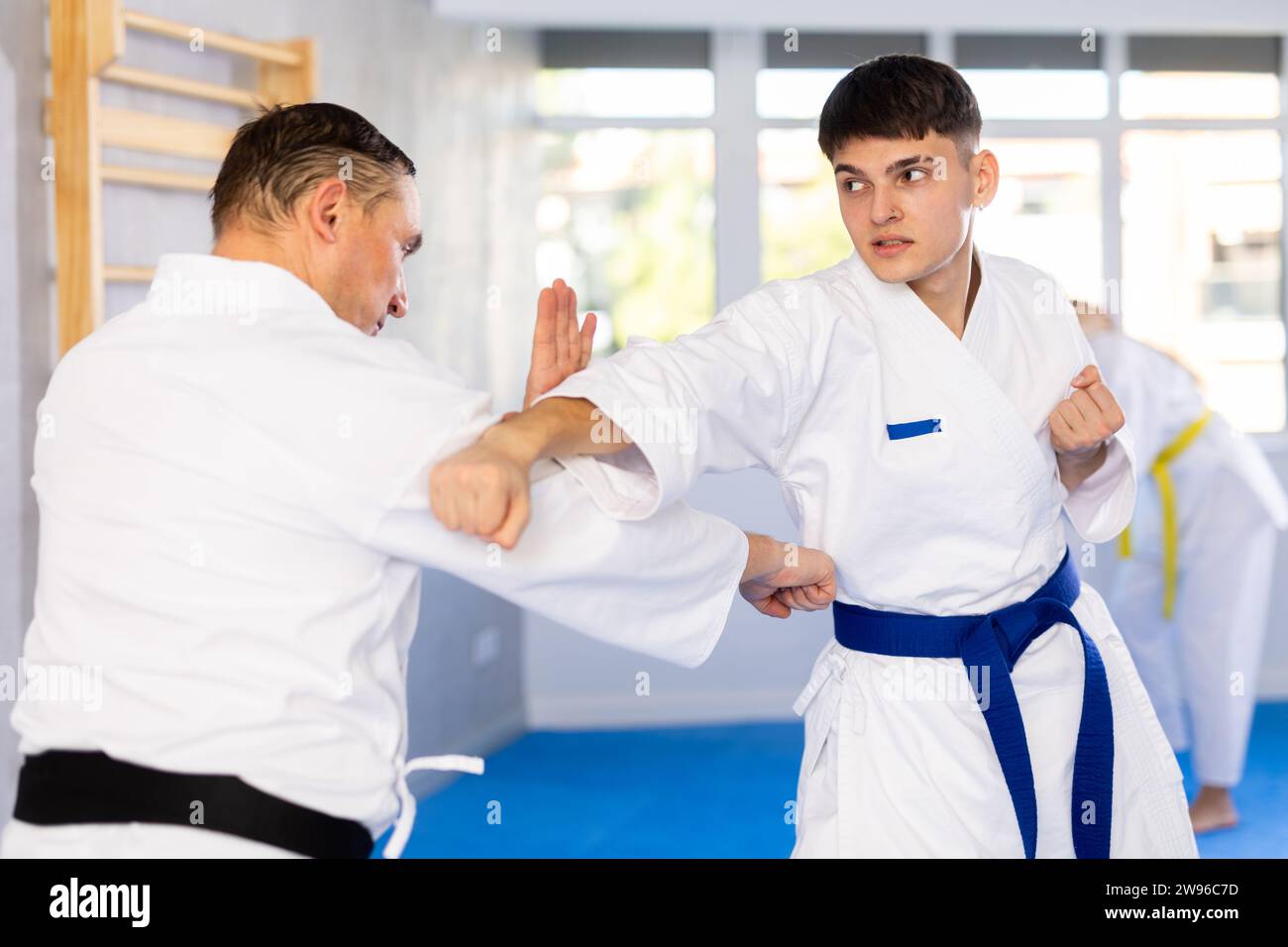 Sportive young guy in kimono applying attack methods on his partner ...