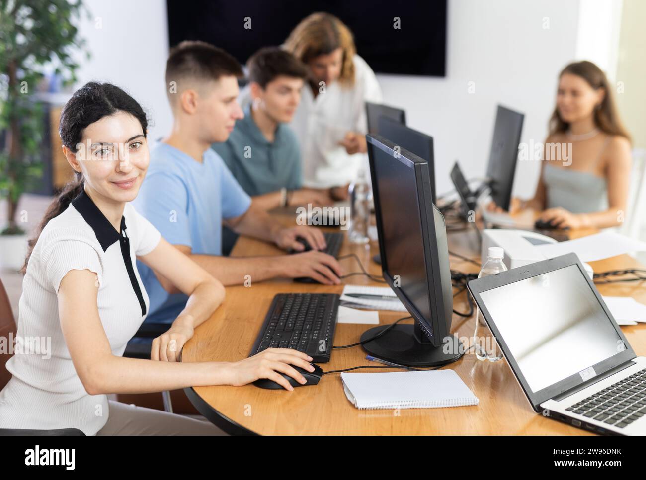 Enthusiastic young girl studying in computer lab with fellow students ...