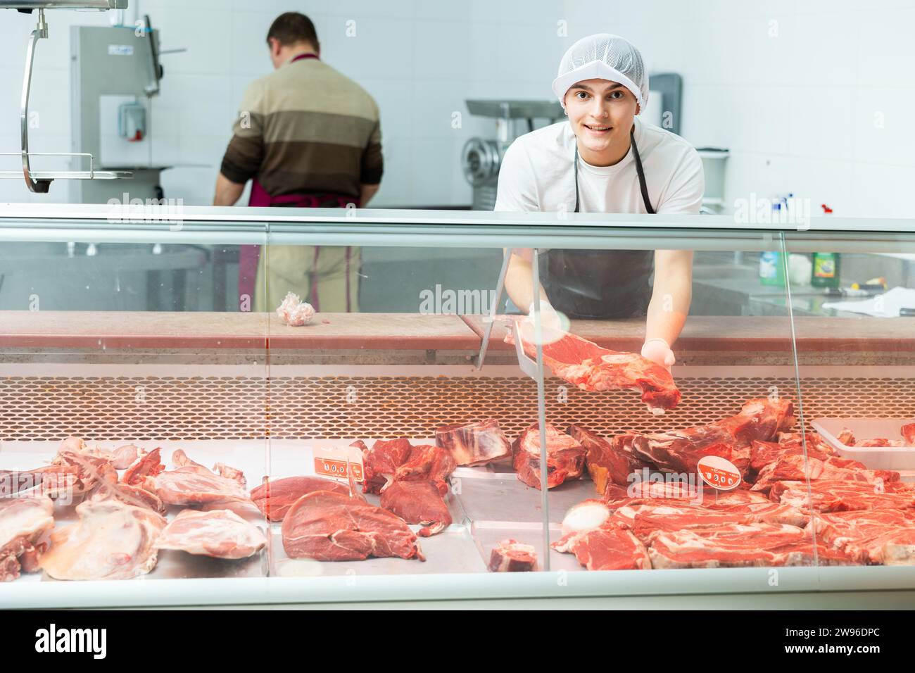 Young guy stands behind counter in meat department of supermarket and ...