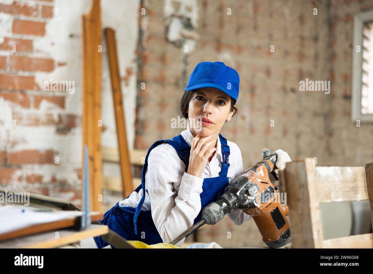 Focused female contractor wearing blue workwear standing with handheld ...