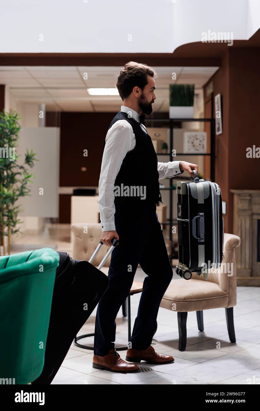 Male hotel concierge carrying bags to help guests in reception area ...